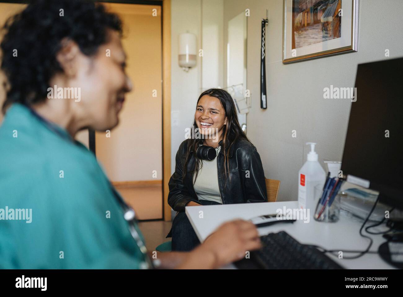 Happy young woman sitting by female doctor at desk in clinic Stock ...