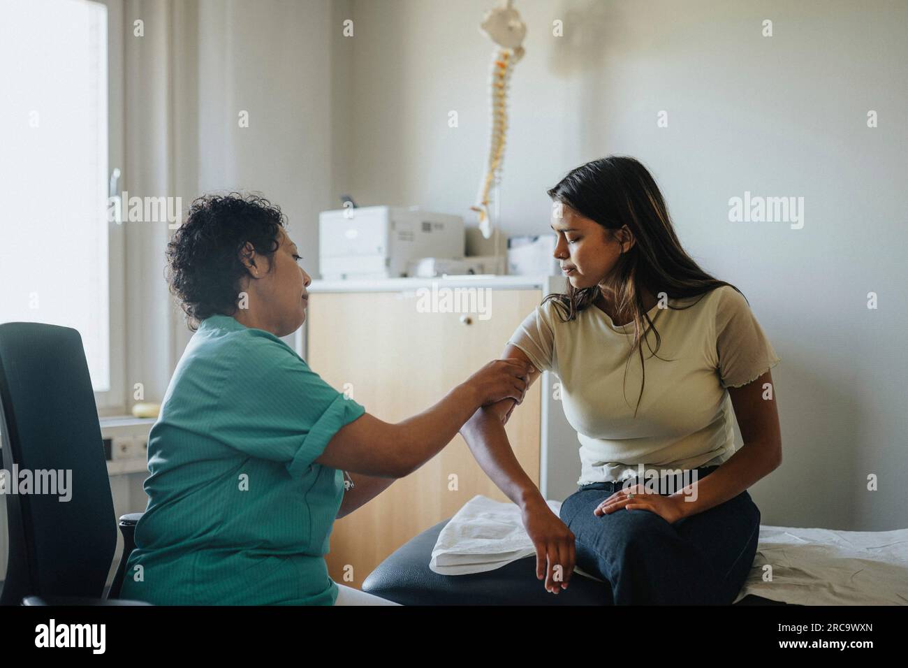 Side view of female doctor examining arm of young woman during medical ...