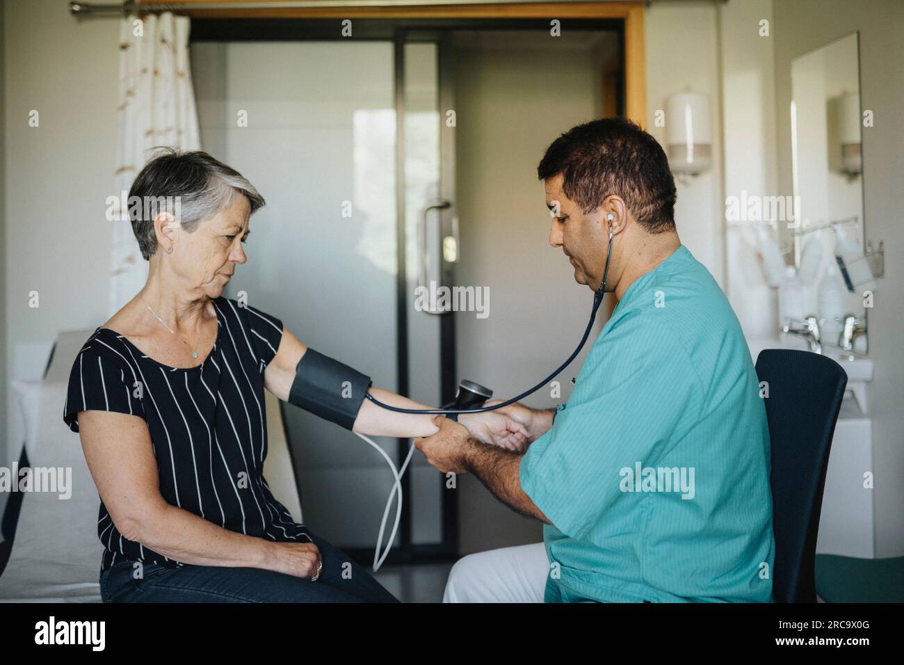 Male doctor checking blood pressure of senior woman while sitting in ...