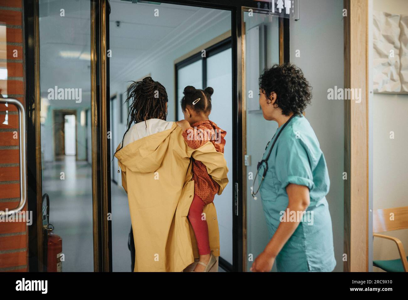 Female doctor walking behind woman carrying daughter while walking in ...