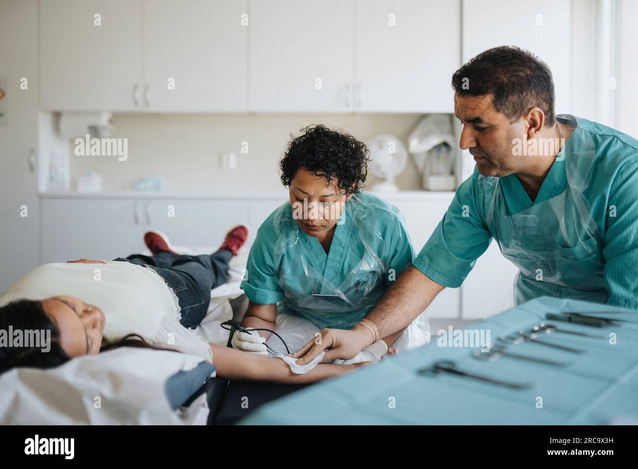 Male and female surgeons operating young woman lying on examination ...