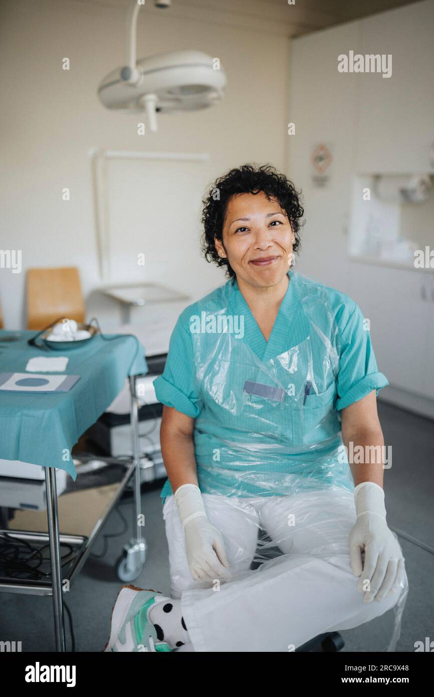 Portrait of smiling female doctor wearing uniform sitting in medical ...