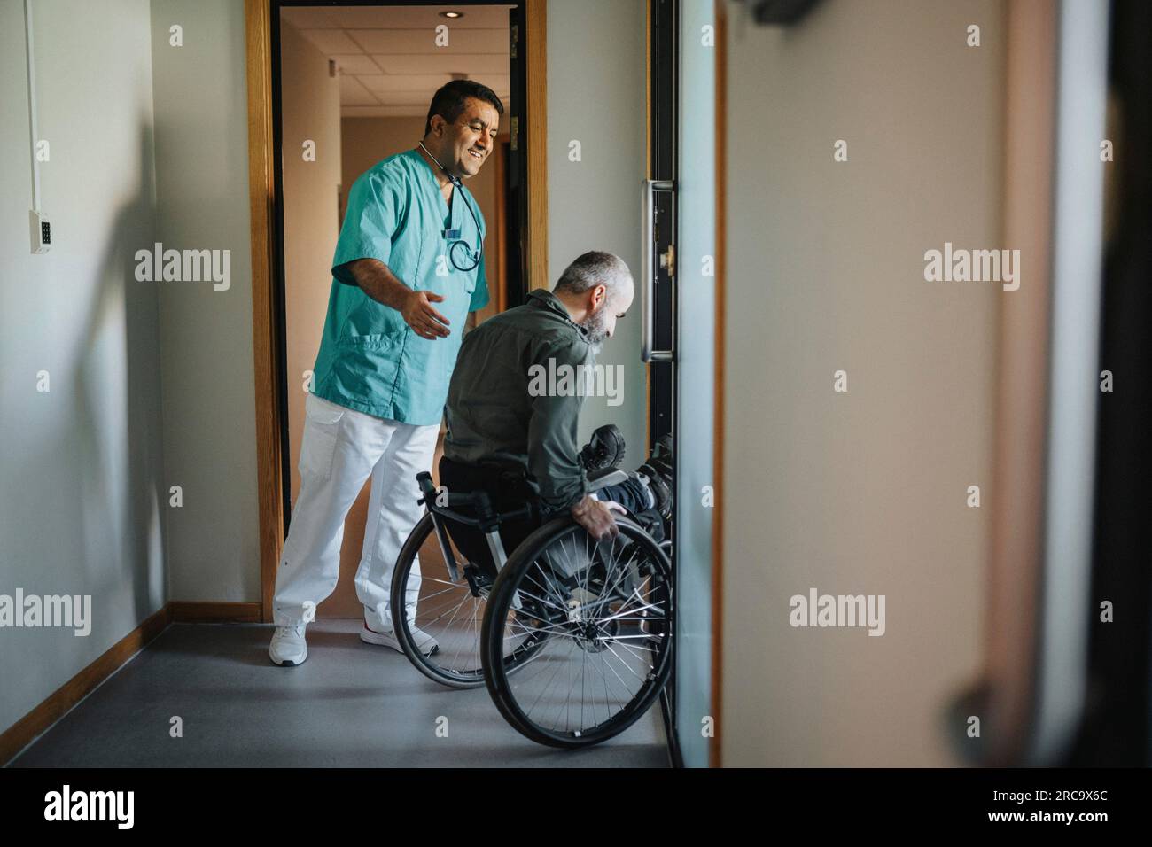 Happy doctor assisting patient in wheelchair at corridor of clinic ...