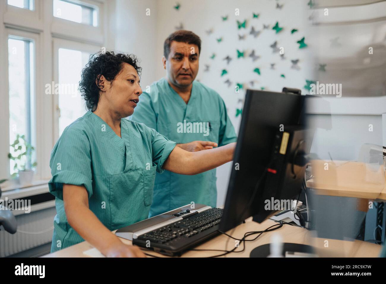 Male and female healthcare workers discussing over computer at ...