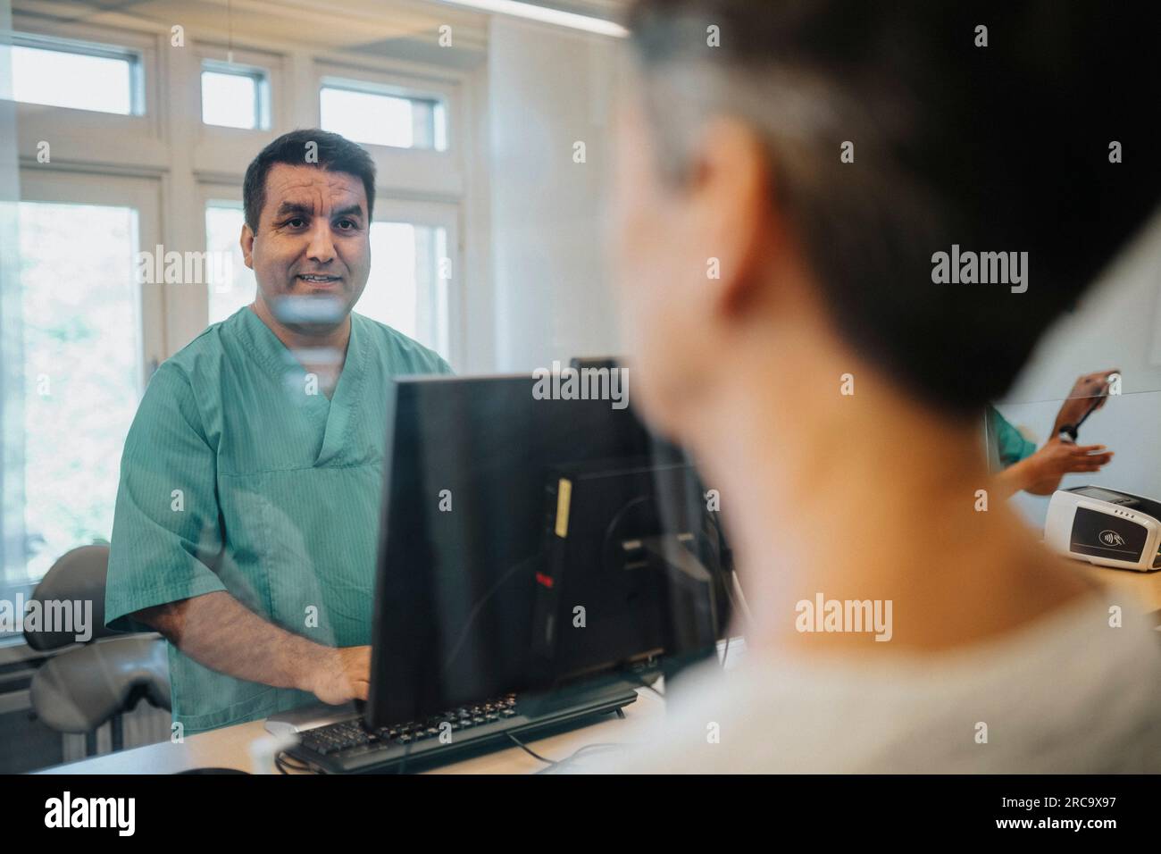 Male receptionist talking with patient through glass screen at ...