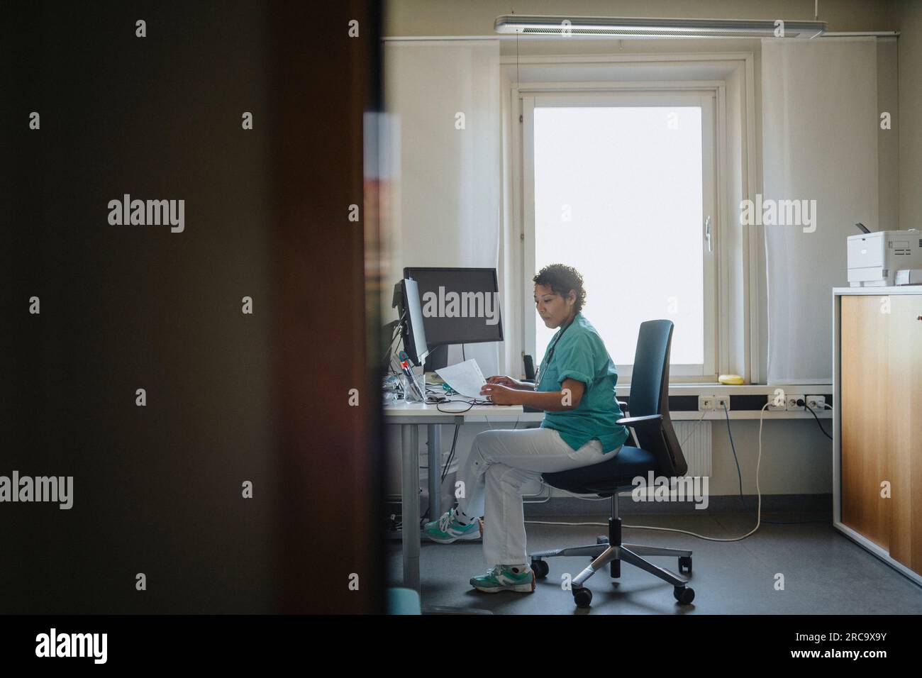 Side view of female doctor checking medical record while sitting at ...