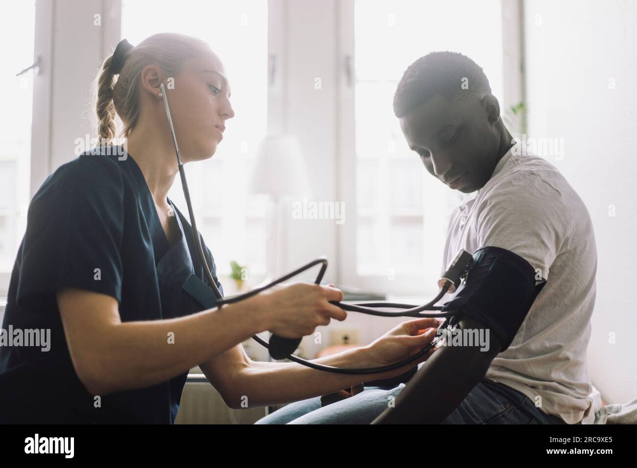 Female nurse checking blood pressure of male teenage patient sitting in ...