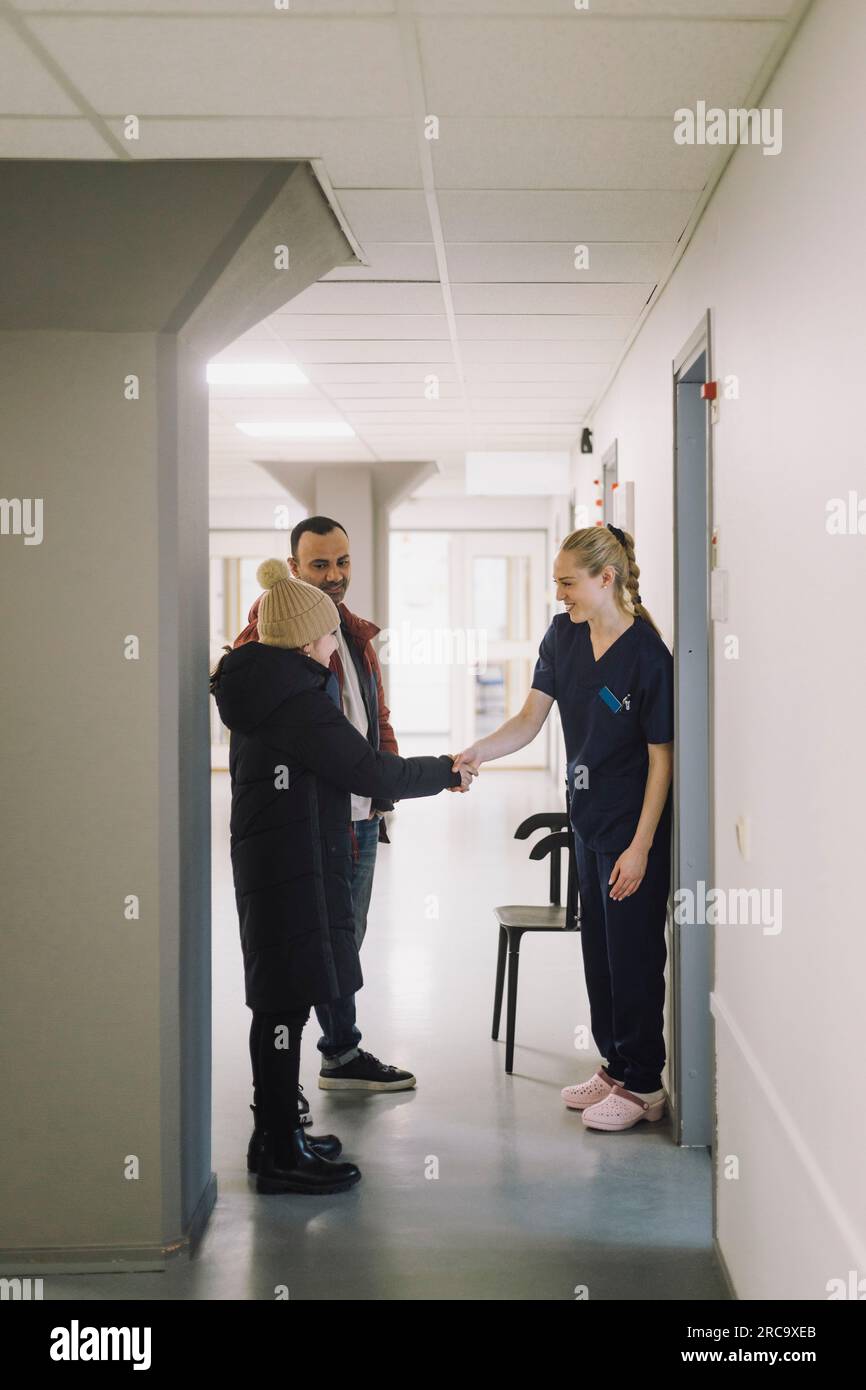 Female nurse shaking hand with girl standing by father at hospital ...