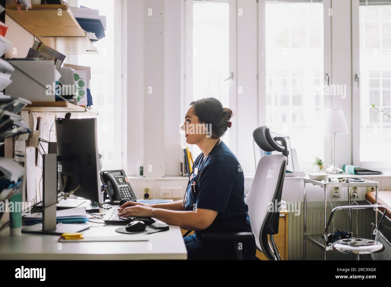 Side view of focused female healthcare worker using computer while ...