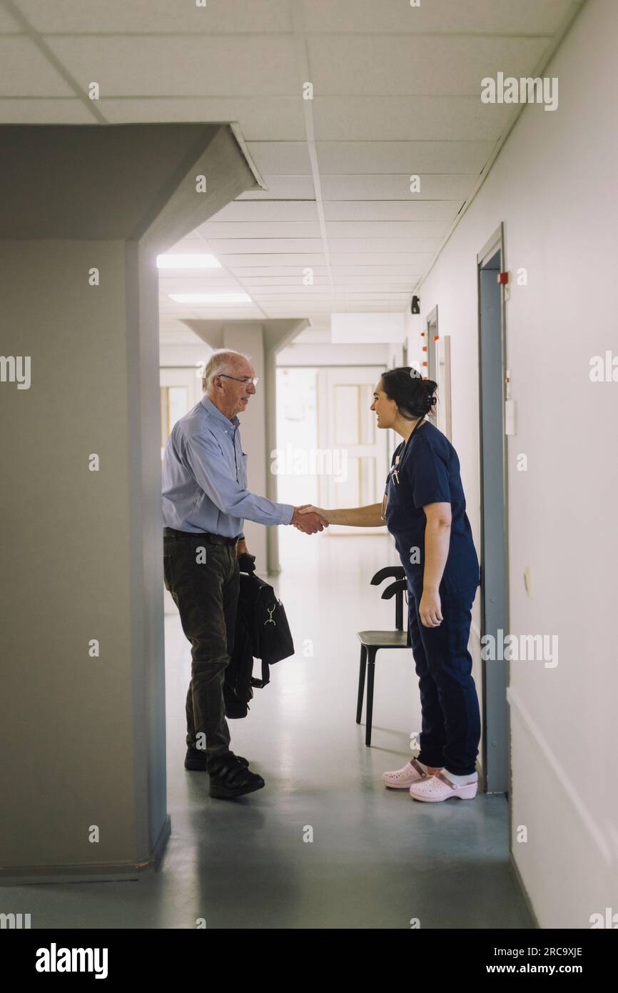 Female nurse doing handshake with male senior patient while standing in ...