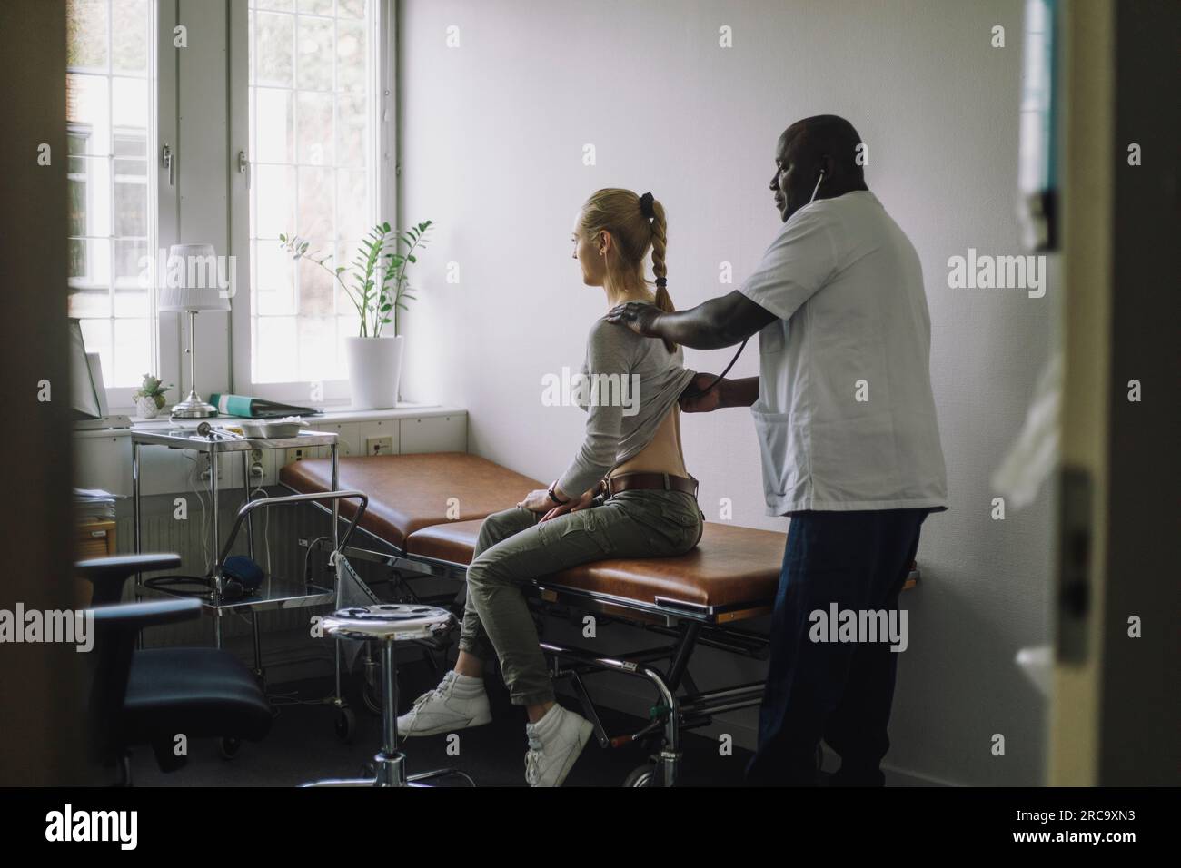 Side view of mature male doctor examining female patient sitting on bed ...