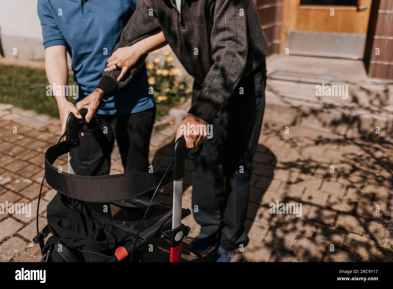 Midsection of female care assistant supporting senior man with walker ...