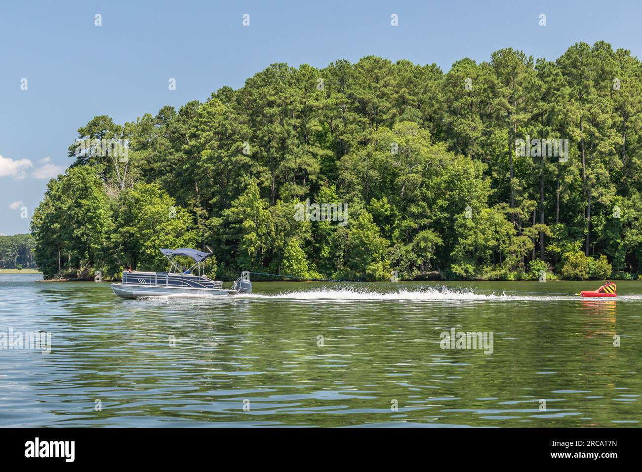 Pontoon boat pulling inflatable tube float raft on lake. Family on a ...