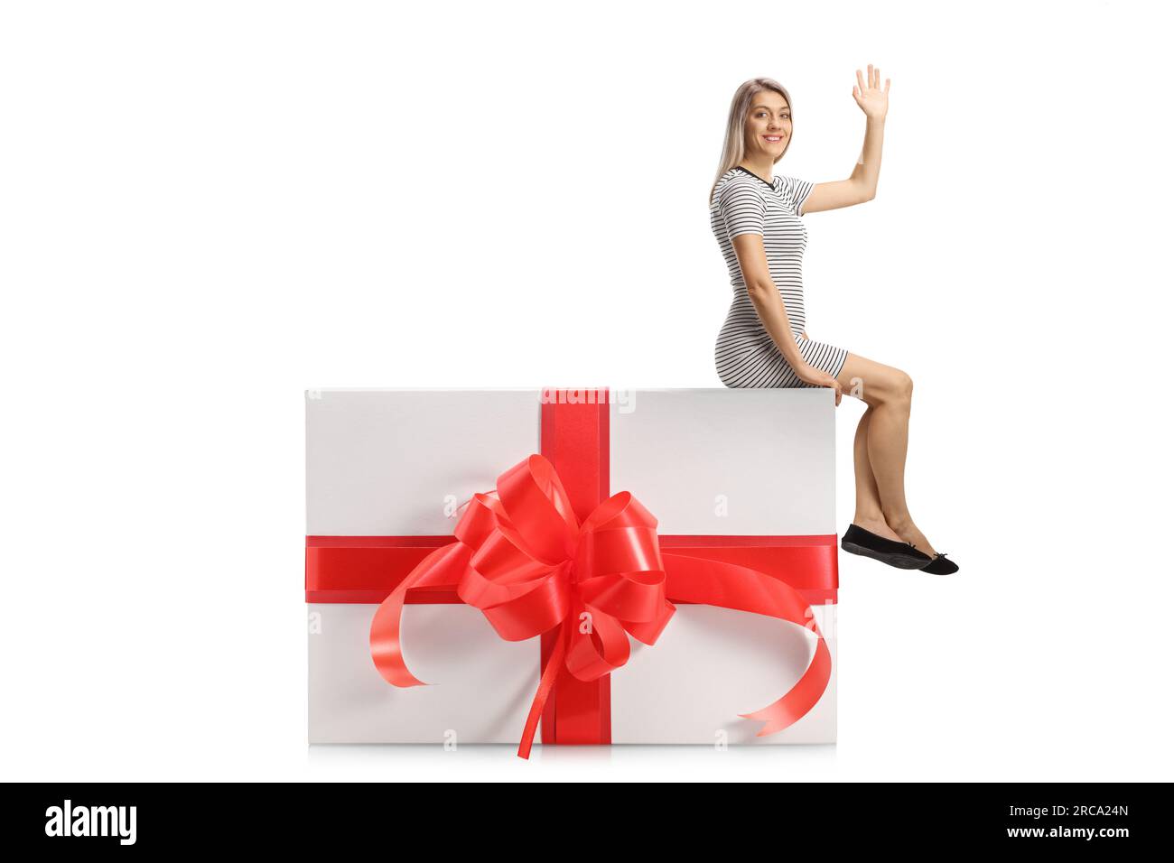 Young woman sitting on a big present box and waving isolated on white ...
