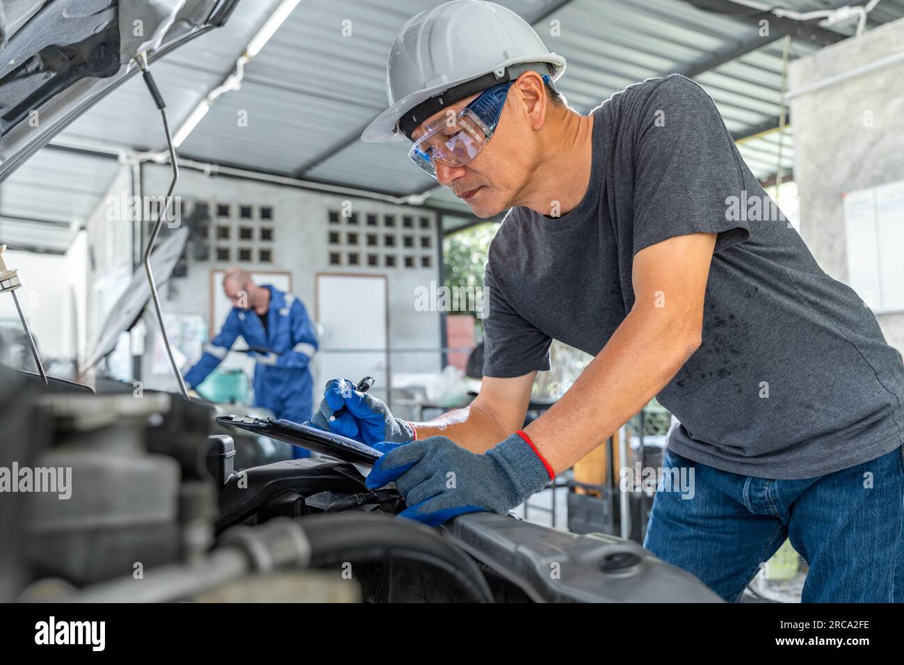 An Asian male car mechanic writing down notes on his notepad while ...