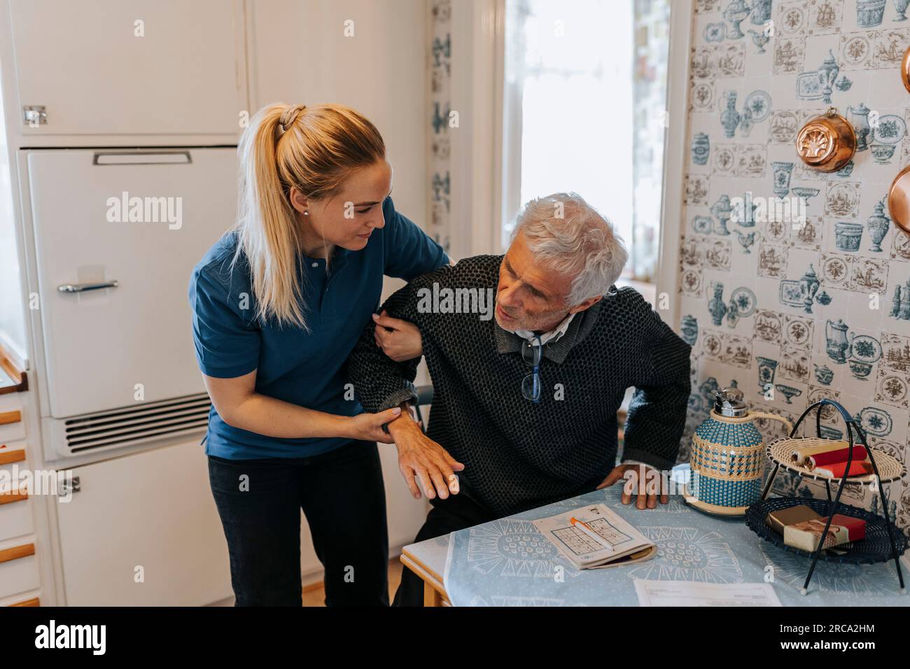 Female caregiver helping senior man in getting up at home Stock Photo ...