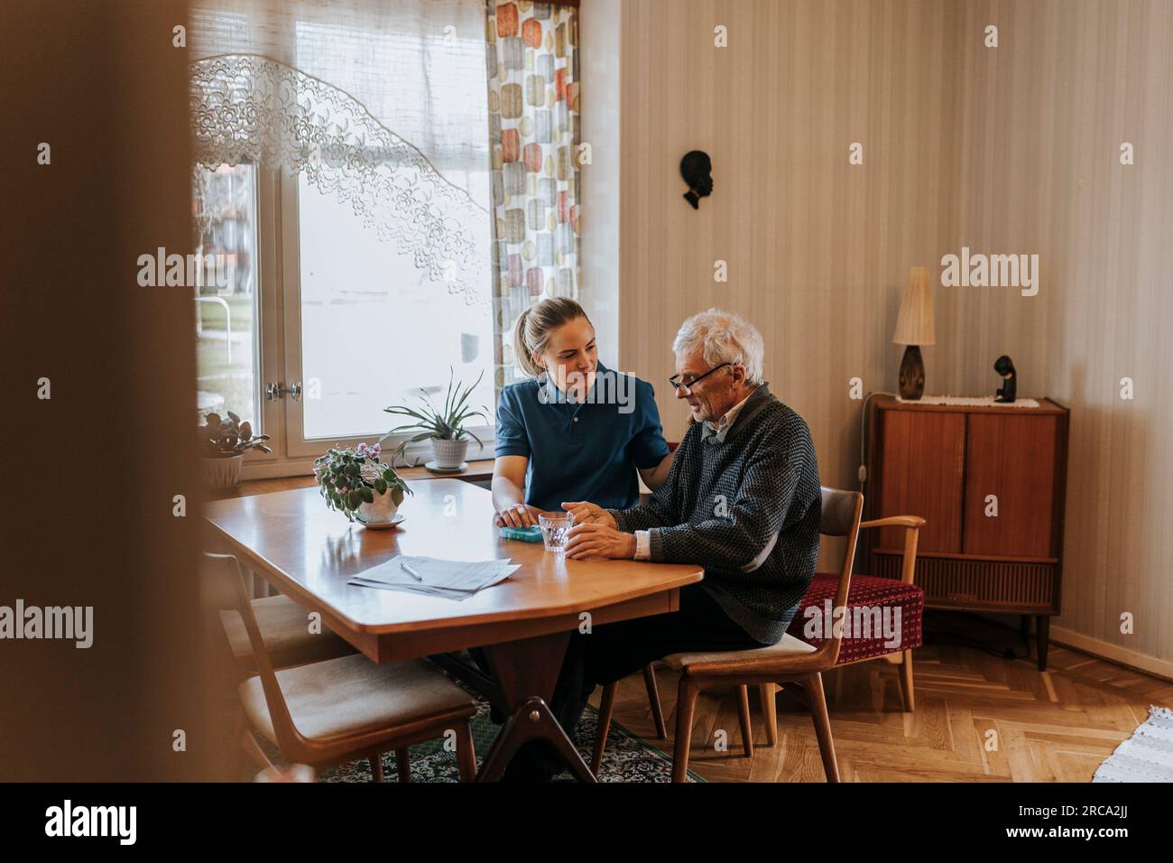 Female care assistant talking to senior man while taking medicine at ...