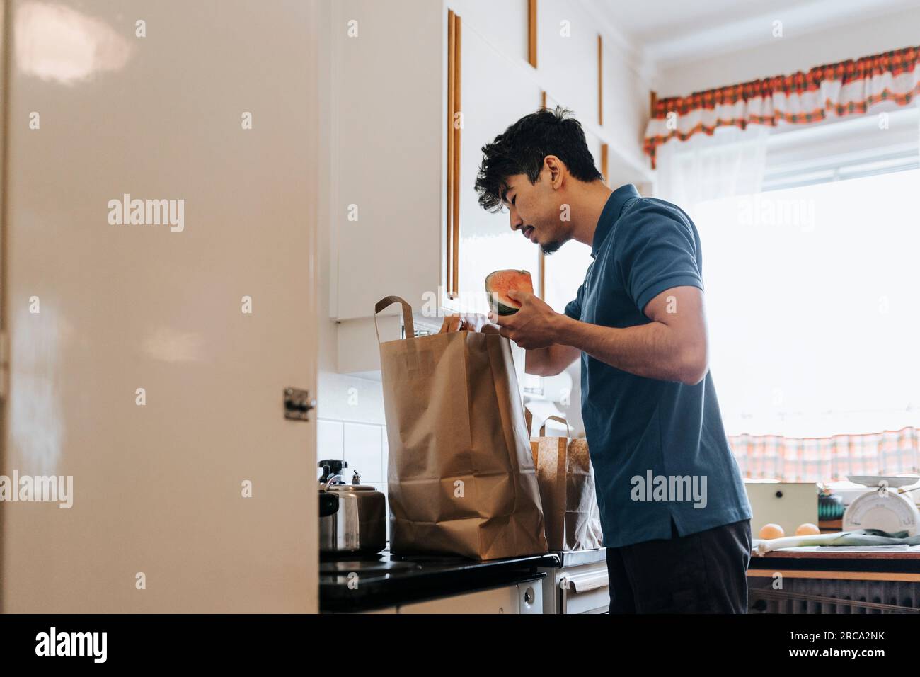 Side view of male care assistant unpacking groceries from bag in ...