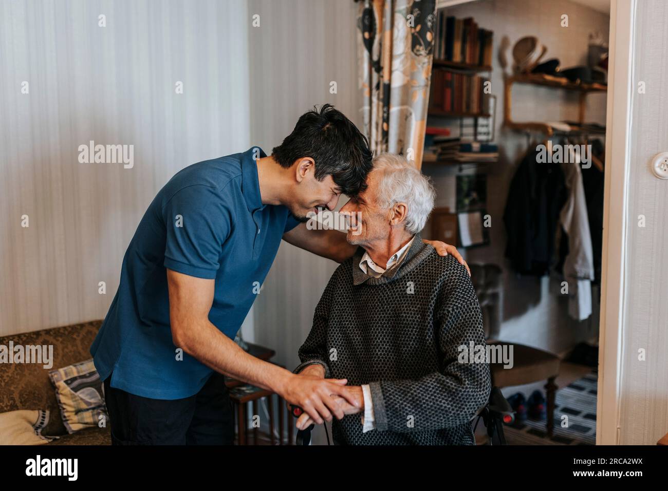 Smiling male care assistant touching forehead with senior man at home ...