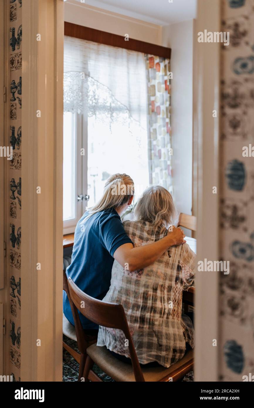 Female care assistant sitting with senior woman on chair at home Stock ...