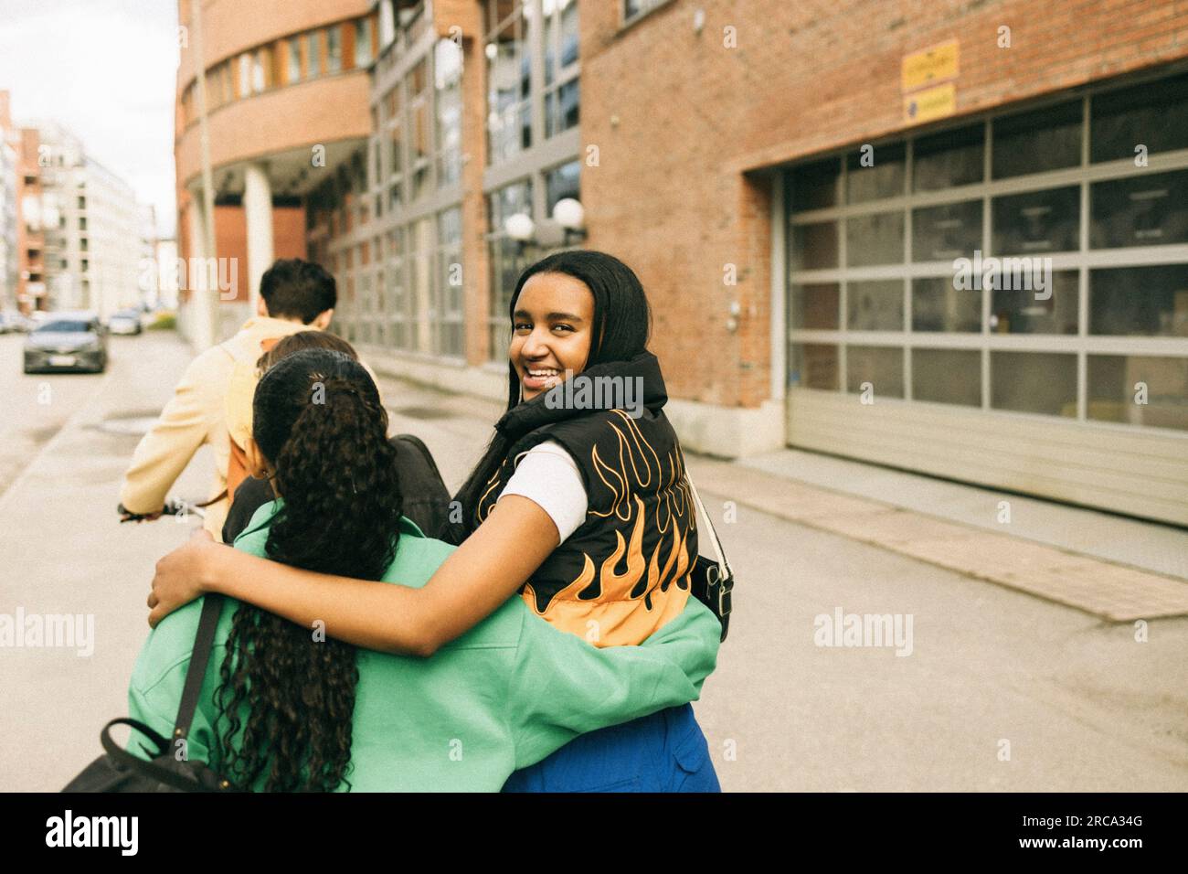 Portrait of smiling young woman looking over shoulder while walking ...