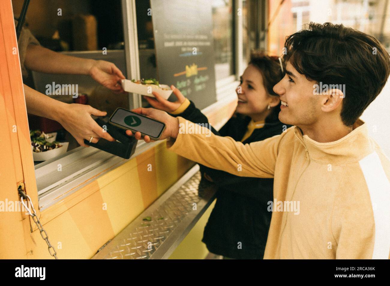 Smiling young man doing online payment while buying food from ...