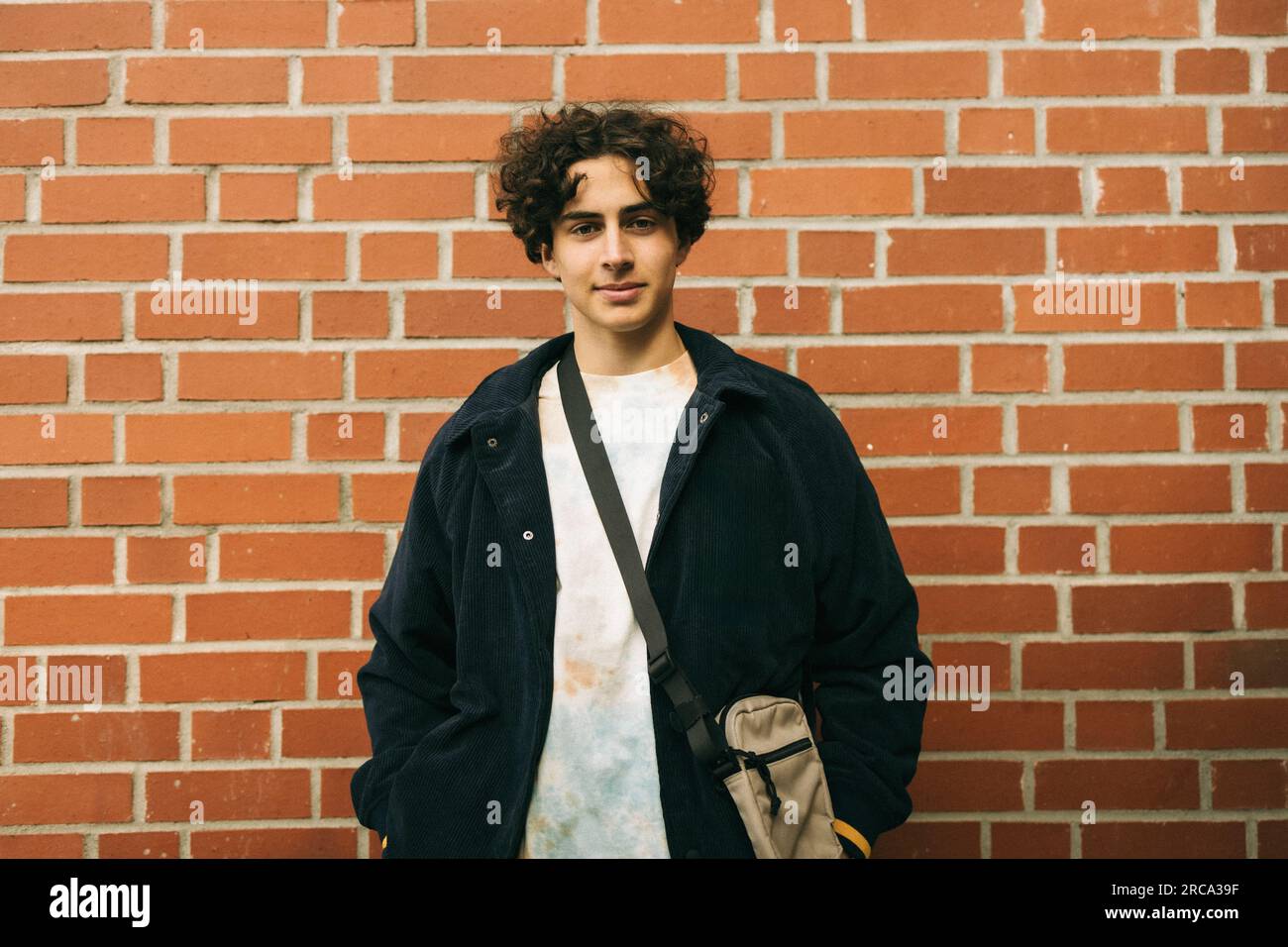Portrait of teenage boy wearing jacket while standing against brick ...