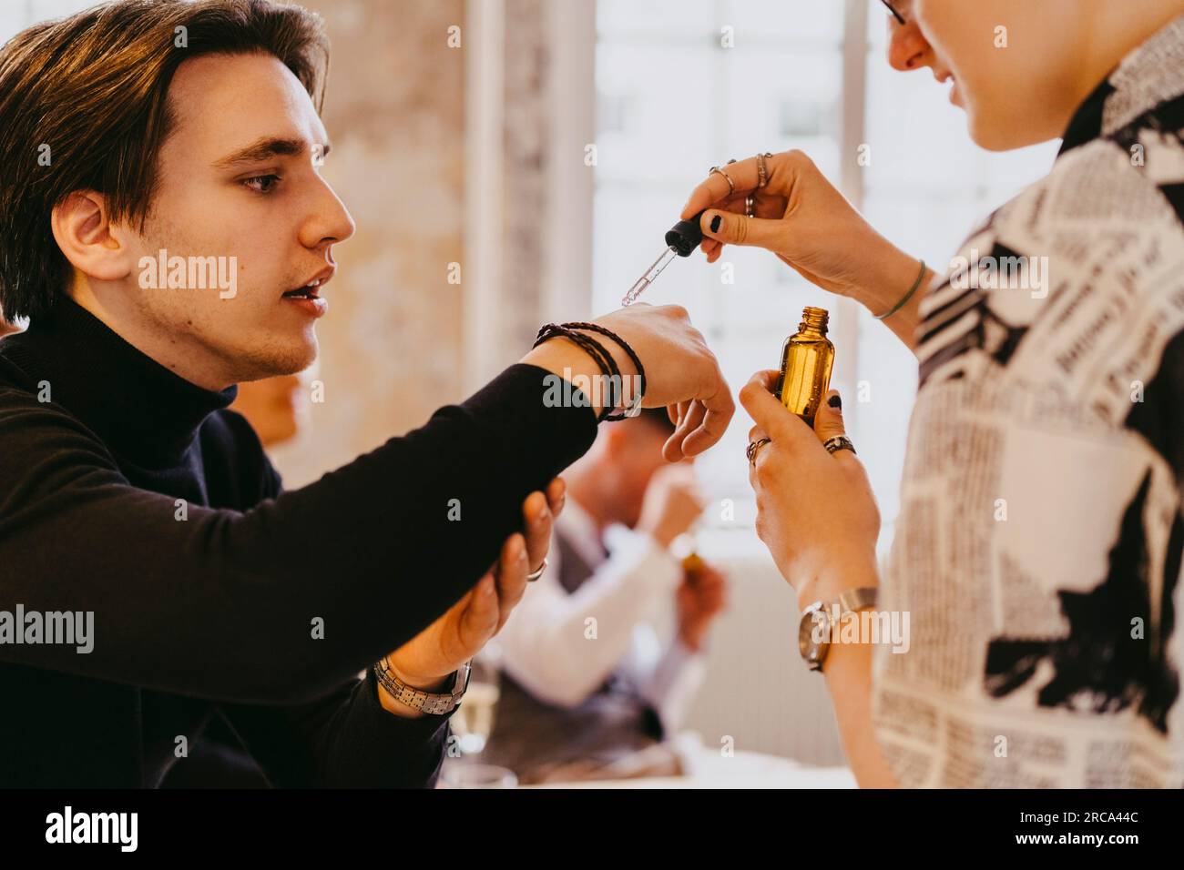 Non-binary person testing essential oil sample on male colleague's hand ...