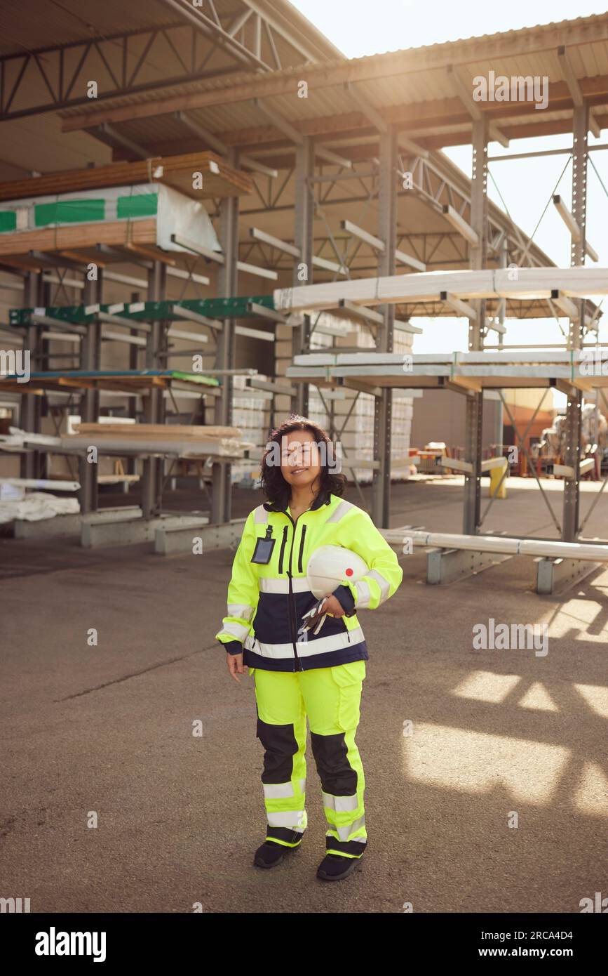 Portrait of female blue-collar worker with hardhat standing outside ...