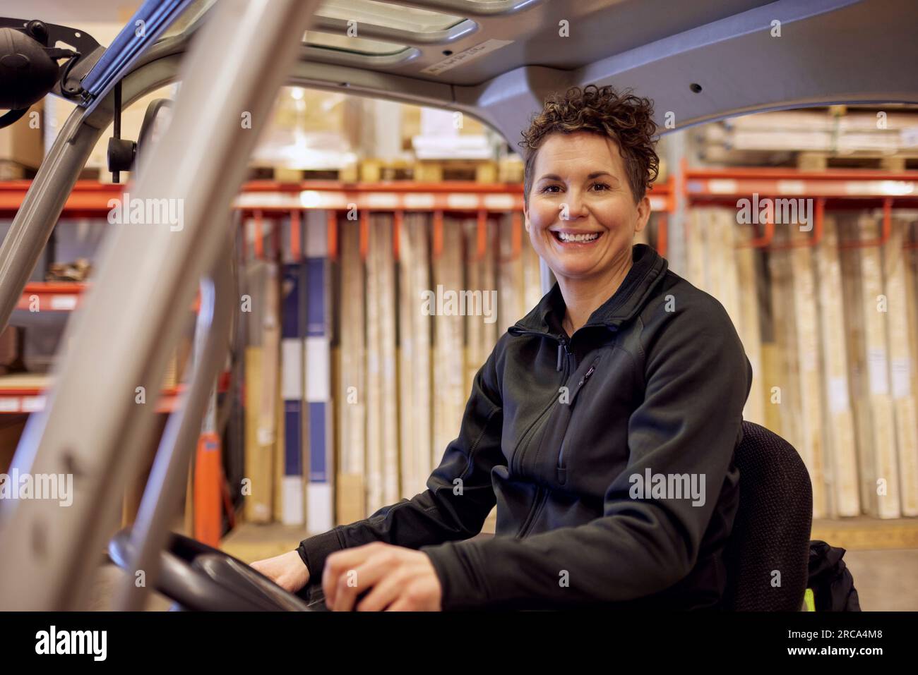 Portrait of smiling female operator driving forklift in lumber industry ...