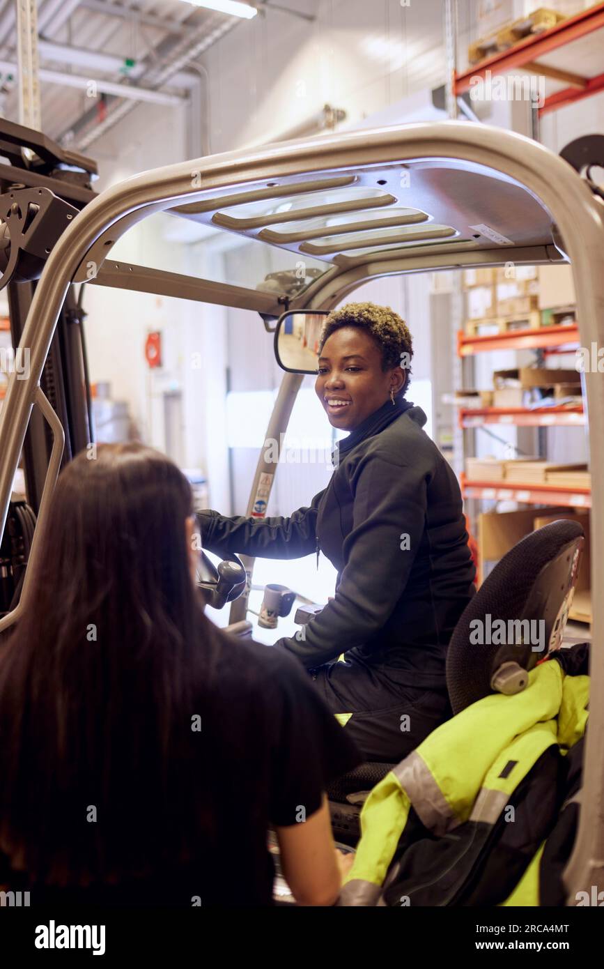 Smiling female forklift operator talking with coworker in distribution ...