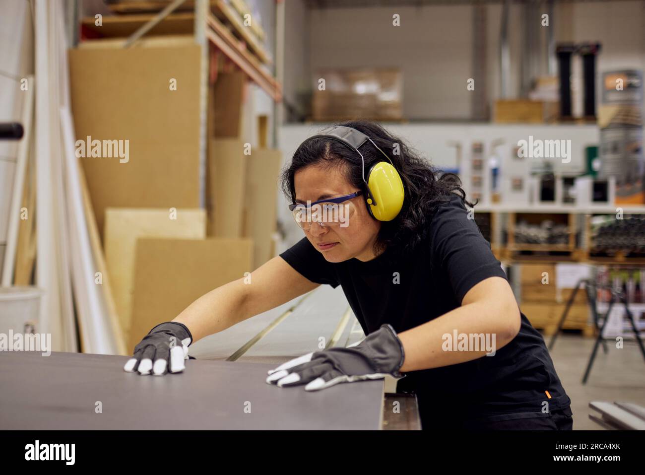 Serious female carpenter wearing protective eyewear and ear protectors ...