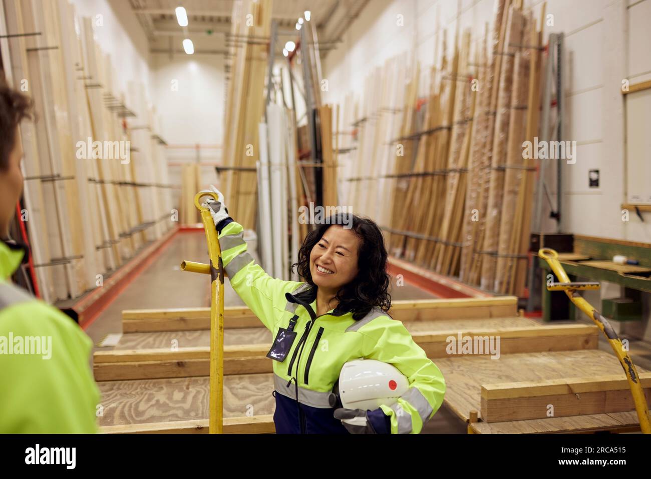 Smiling blue-collar worker discussing with colleague in lumber industry ...