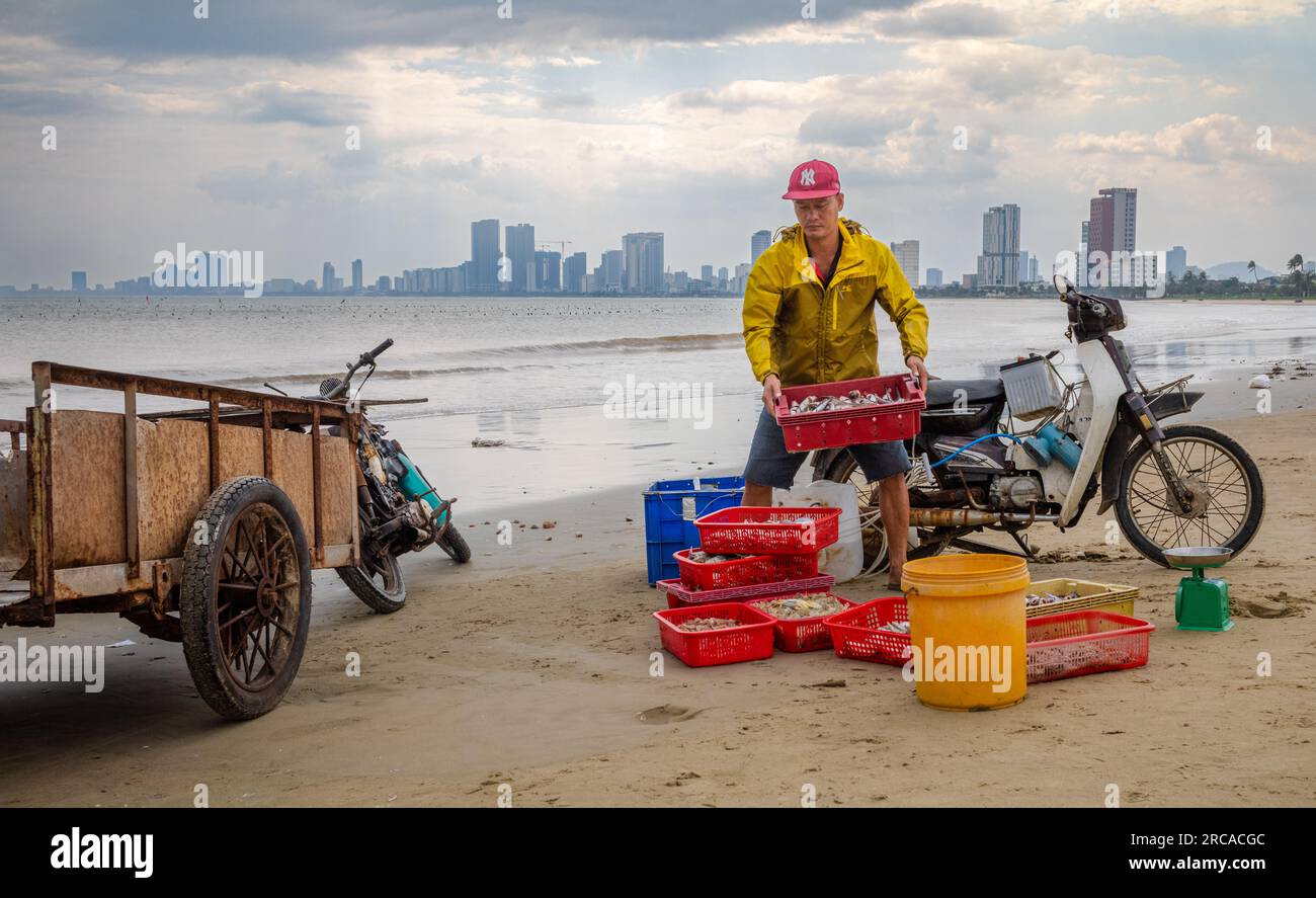 A fisherman lifts a tray of fish and seafood next to a rusty scooter on ...