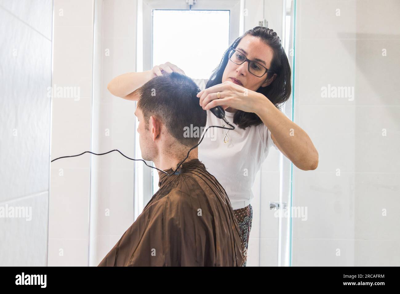 Woman giving Caucasian man a haircut in a home setting. Family and ...