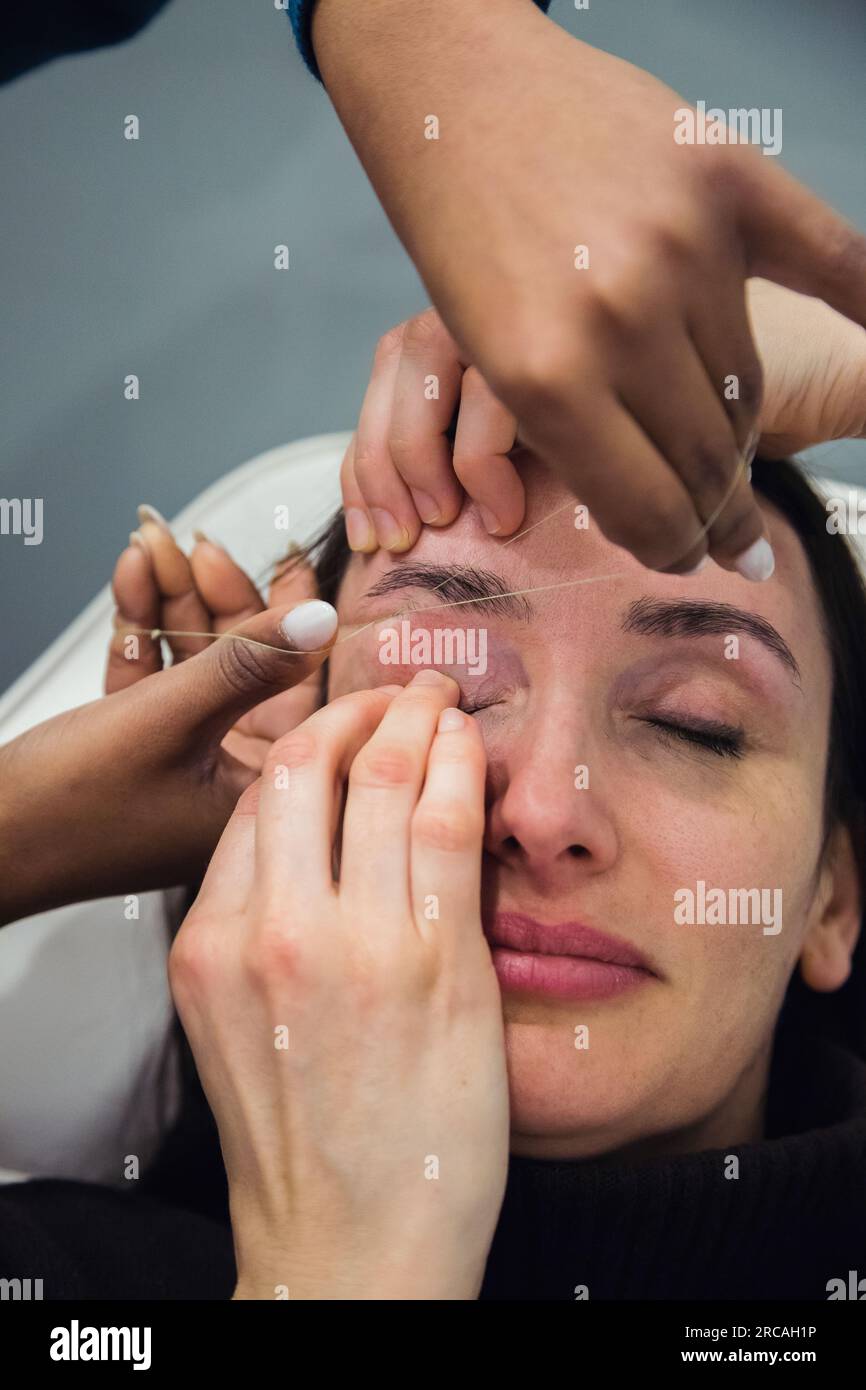 Caucasian woman removing hair from eyebrows with thread technique done ...