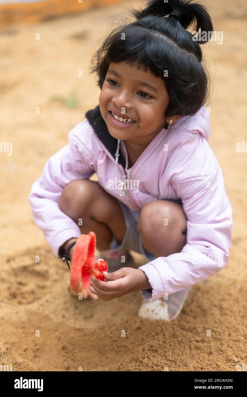 A small girl is having a blast playing in the mud. She is covered in ...