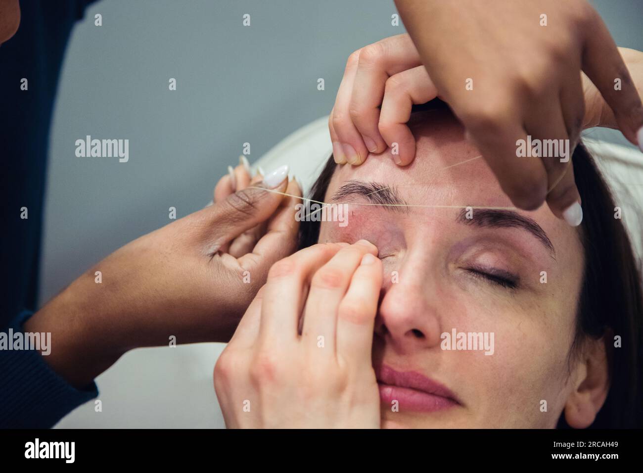 Caucasian woman removing hair from eyebrows with thread technique done ...