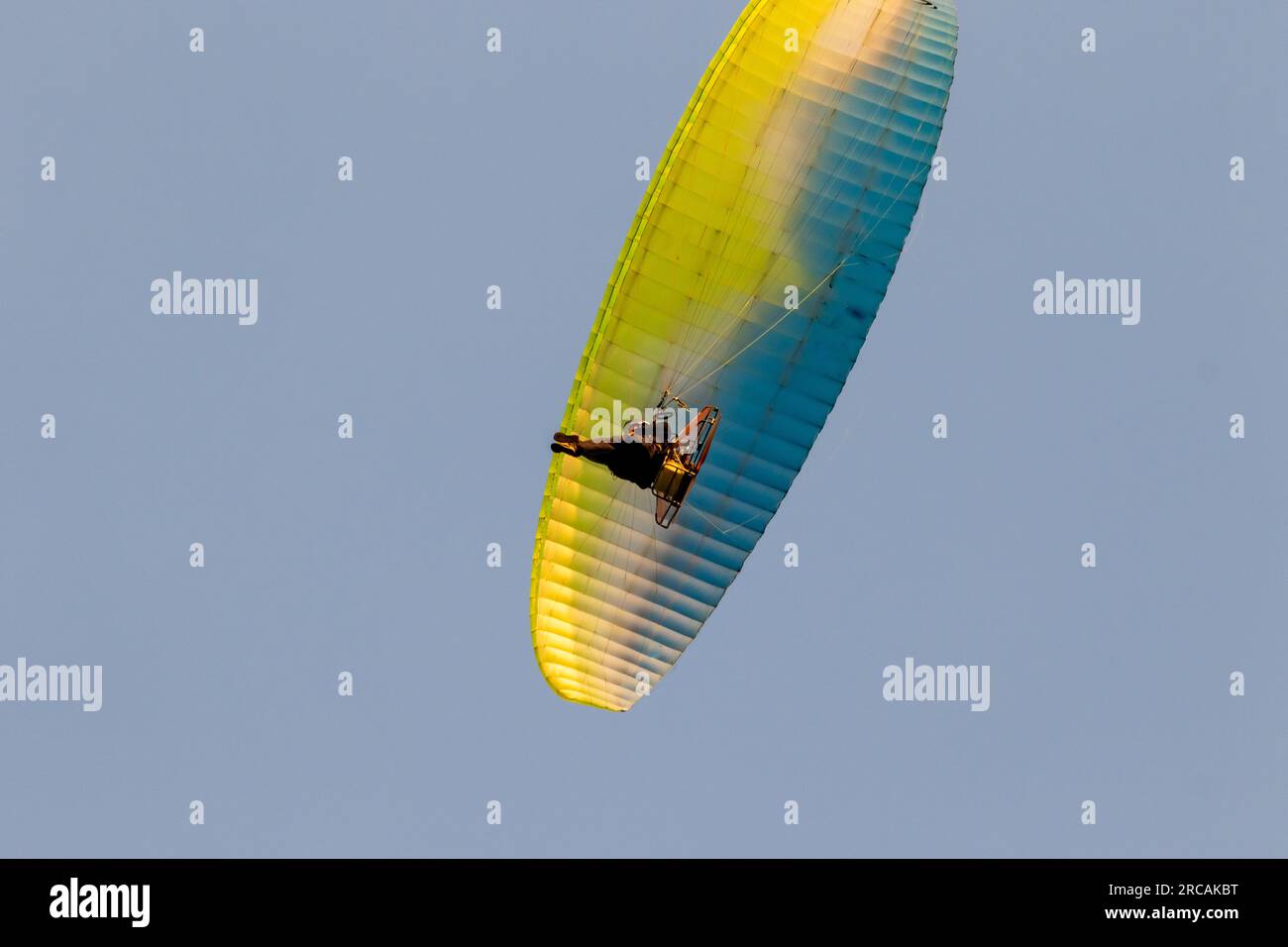 A powered paraglider with blue and yellow canopy and blue sky ...