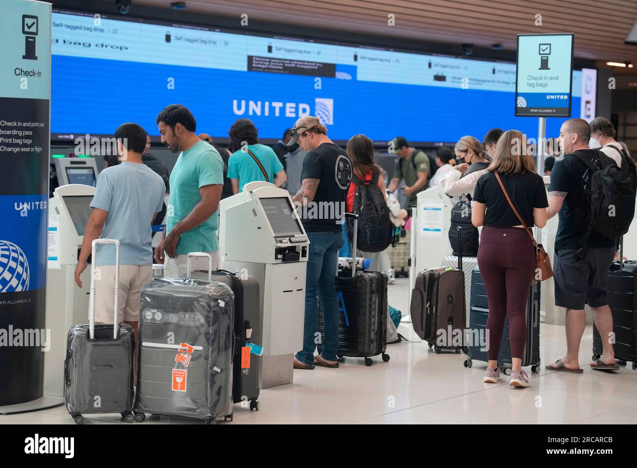 Travelers queue up at self check-in kiosks at the United Airlines ...