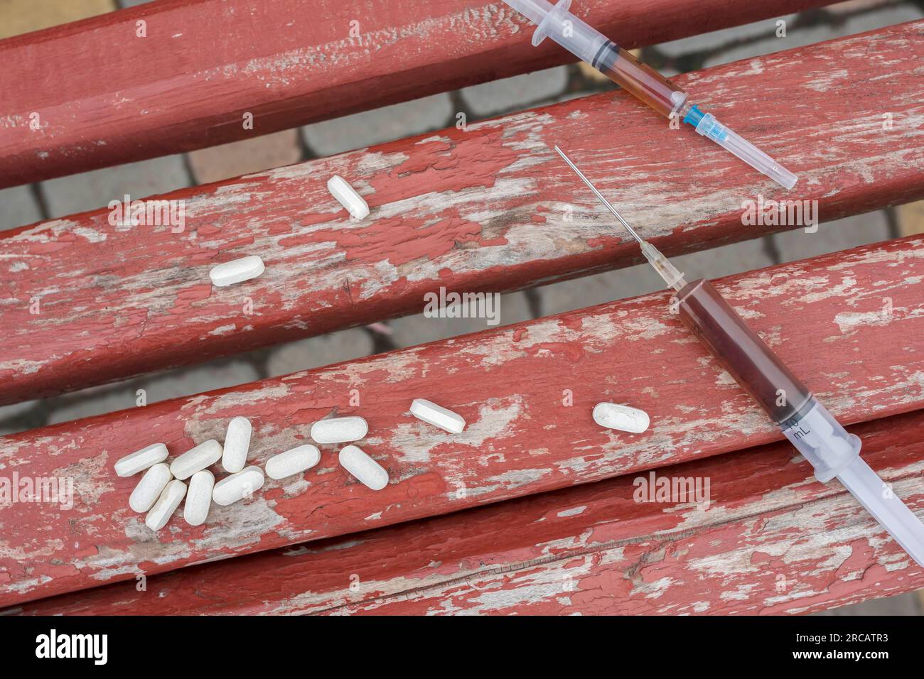 Addiction and drug abuse concept. Syringes and pills on a bench, close ...