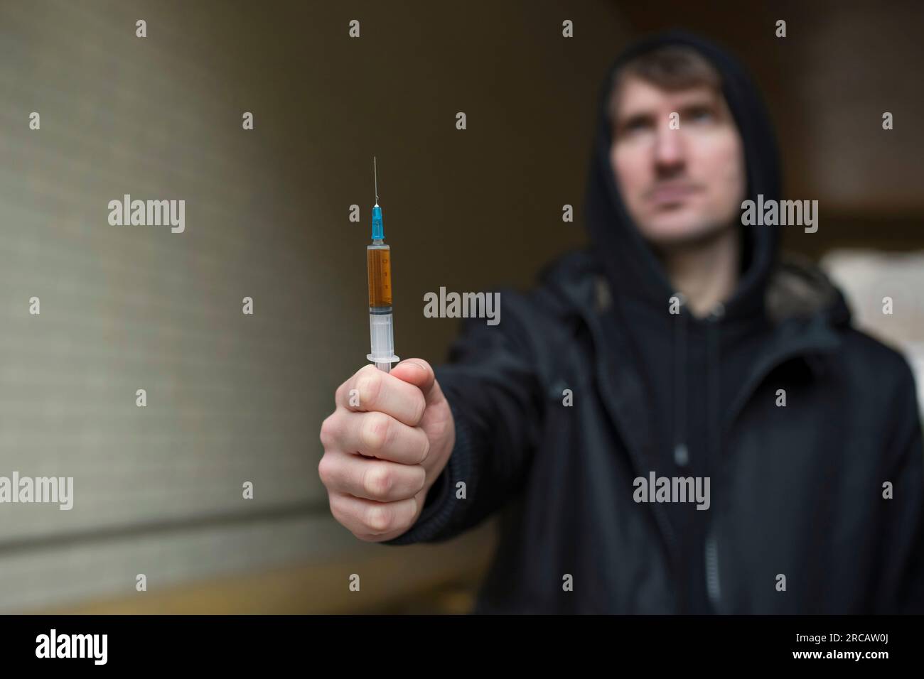 Addict with a syringe in his hand in a dark passage. Addiction concept ...