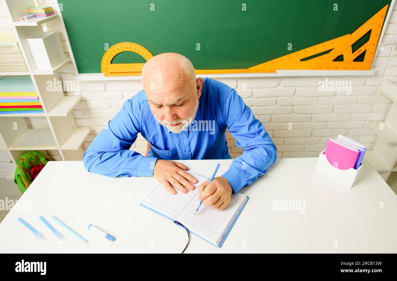Teacher starts lesson. Male teacher working at table in classroom. Test ...