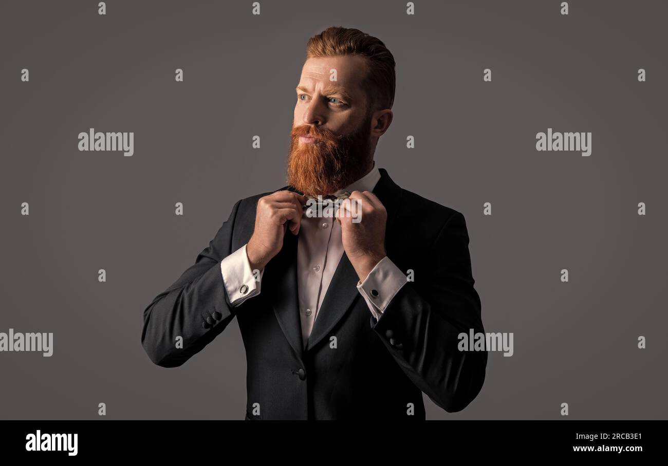 Elegant man fixing bowtie in black tuxedo. Handsome man with red beard ...