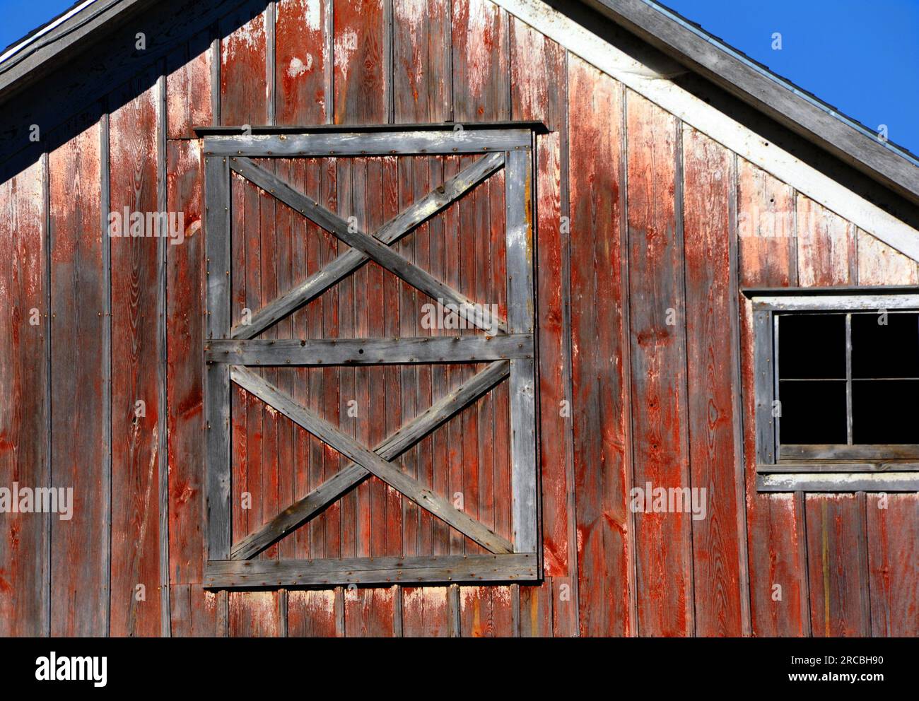Red wooden loft door, in Kansas, is closed. Paint is worn and cracked ...