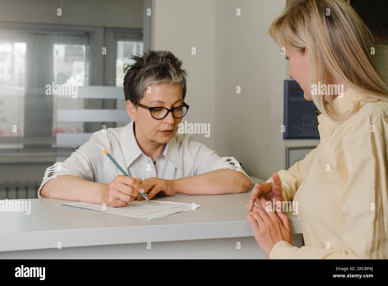 Patient at reception desk of clinic talking about her appointment ...