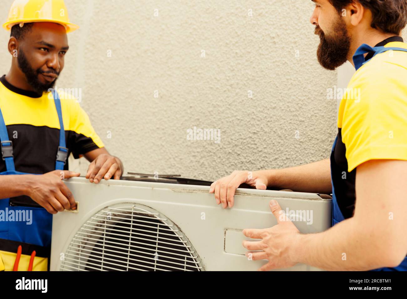 African american repairman and apprentice worker pulling apart old defective outdoor hvac system ...