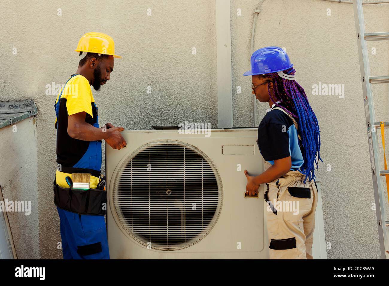 African american engineering coworkers opening up rusty out of service air conditioner to ...