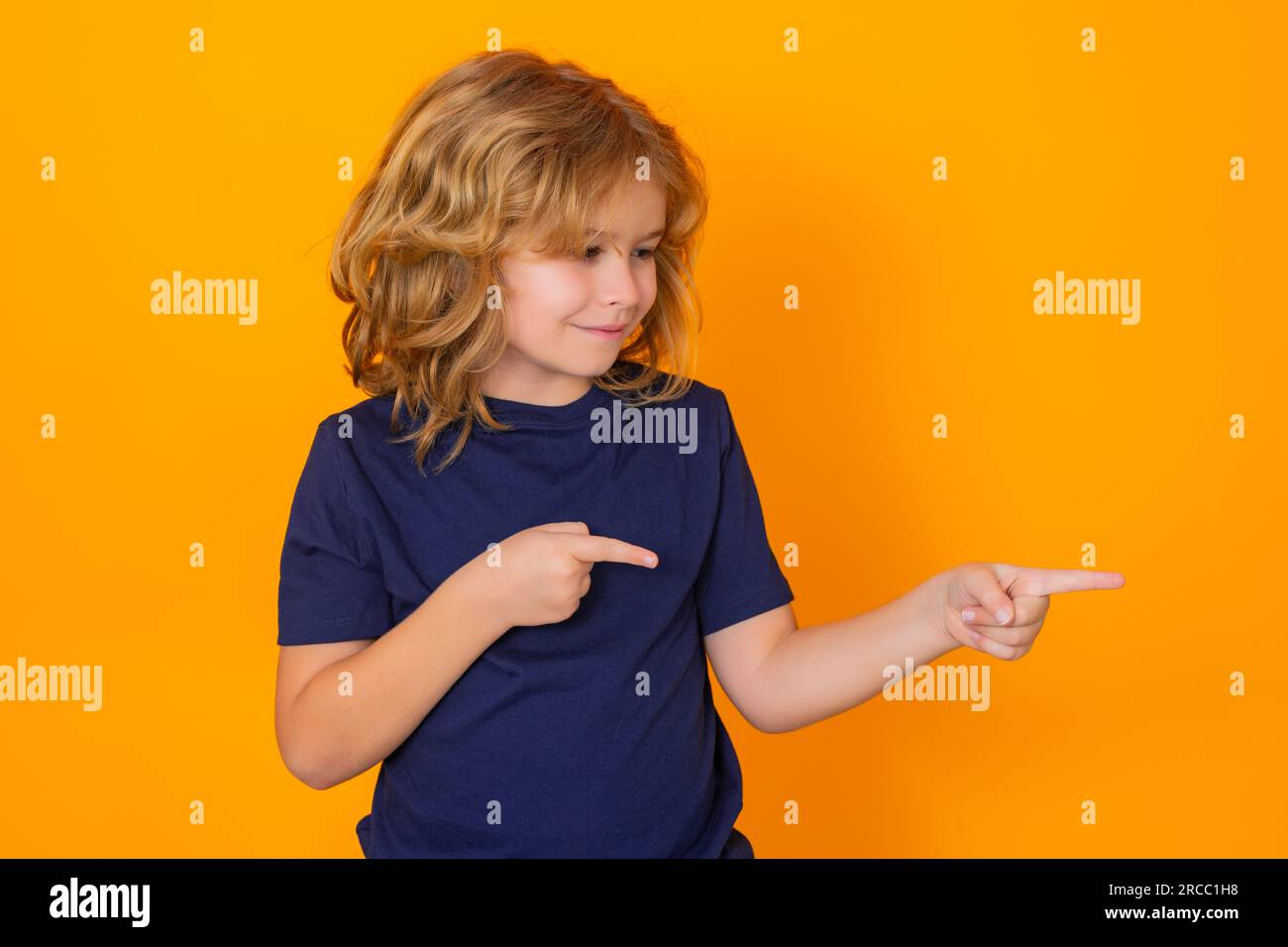 Child boy pointing finger away on yellow isolated studio background ...