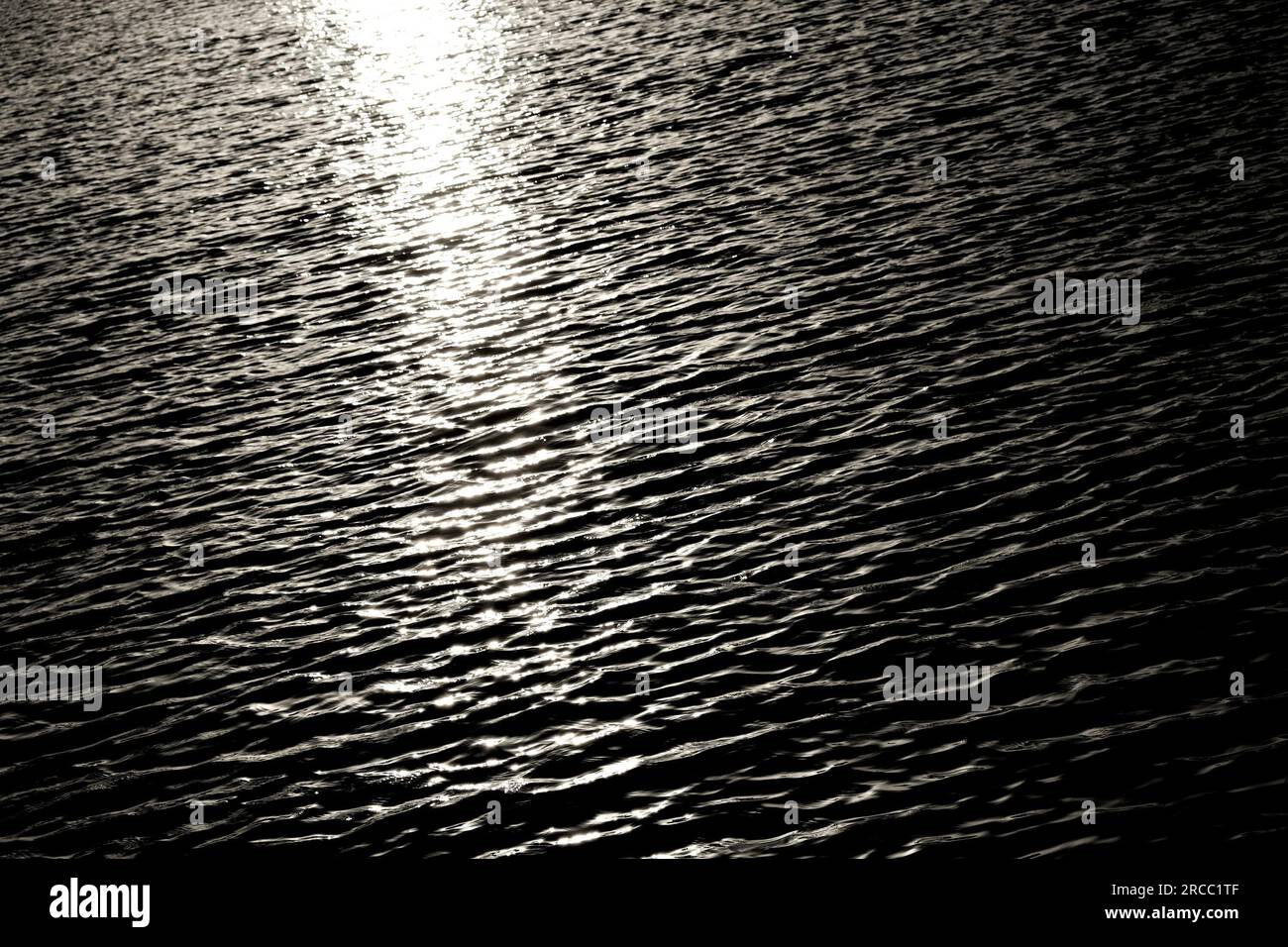 Water surface with wavelets and sun reflections, dark tone image with ...